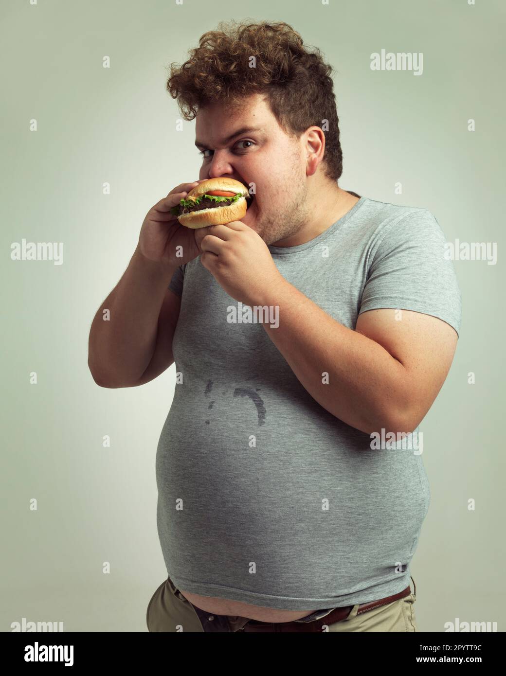 Dont come near my burger. Studio shot of an overweight man biting into ...
