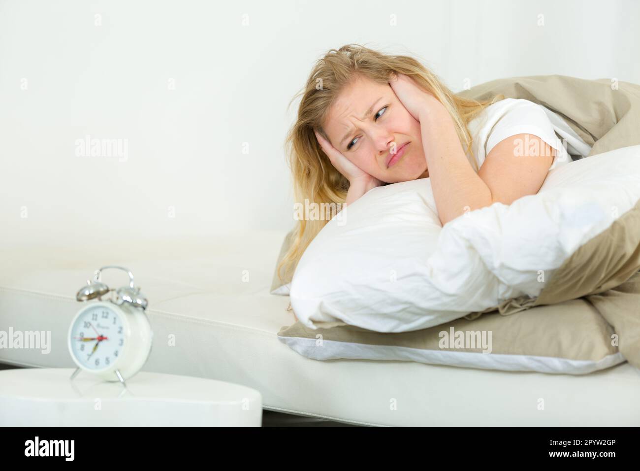 woman in bed covering her ears from alarm clock bell Stock Photo - Alamy