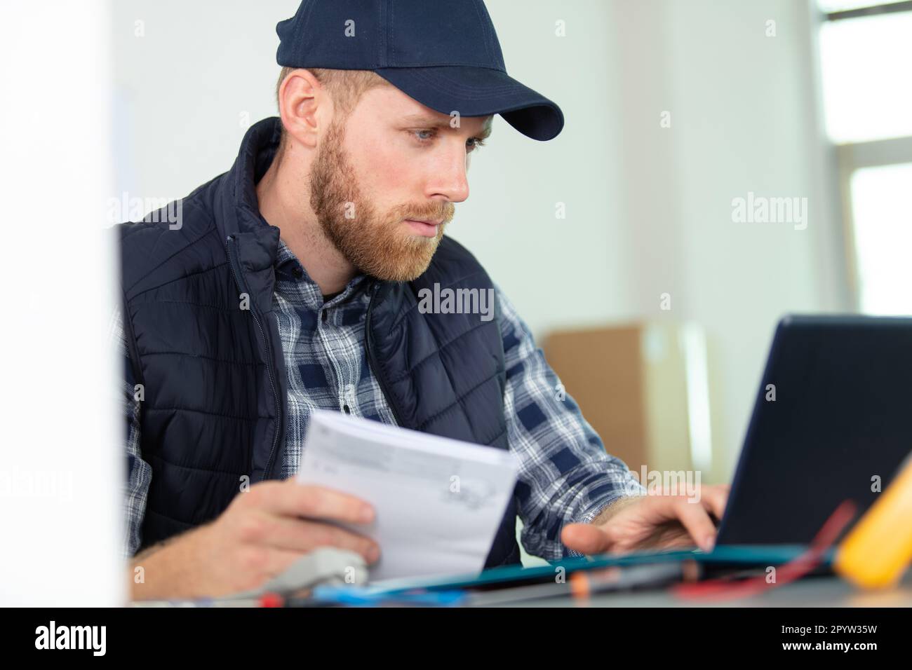 man in cap reading instructions and using laptop computer Stock Photo ...