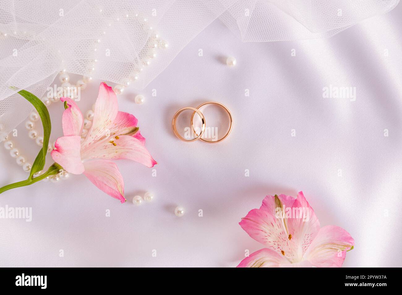 Two gold wedding rings lie on a white satin background with a ...