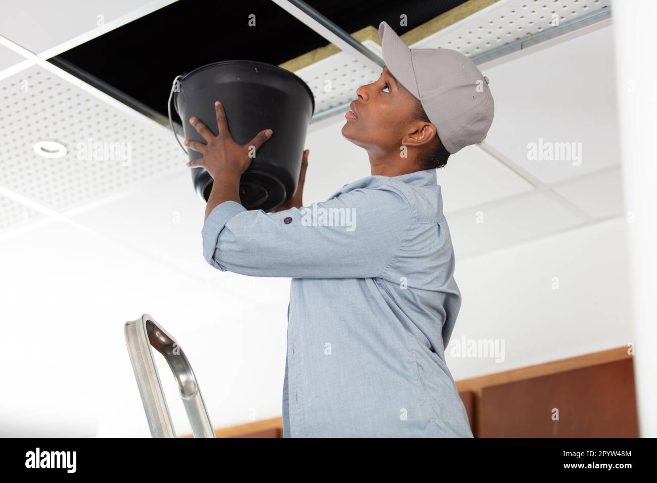 woman holding bucket under an open ceiling panel Stock Photo - Alamy