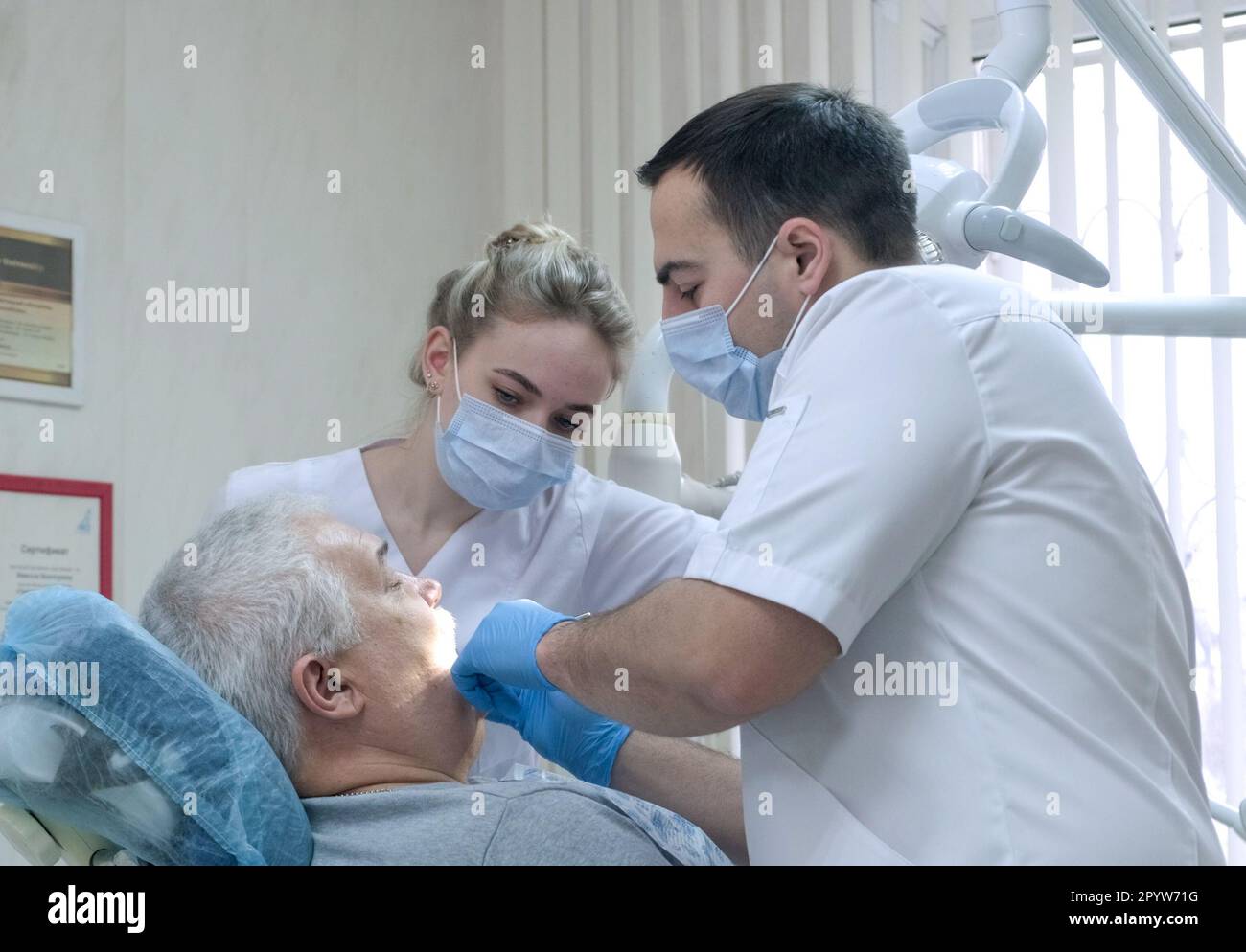 Male dentist with nurse in protective masks working with patient in ...
