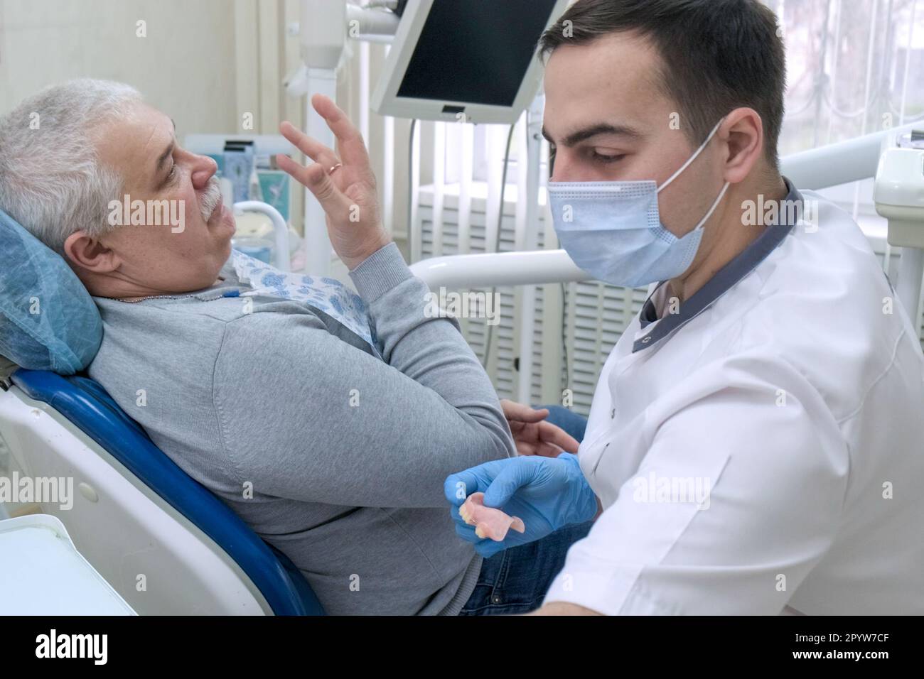 Senior man sitting in dentist chair talks about his dental problems to ...