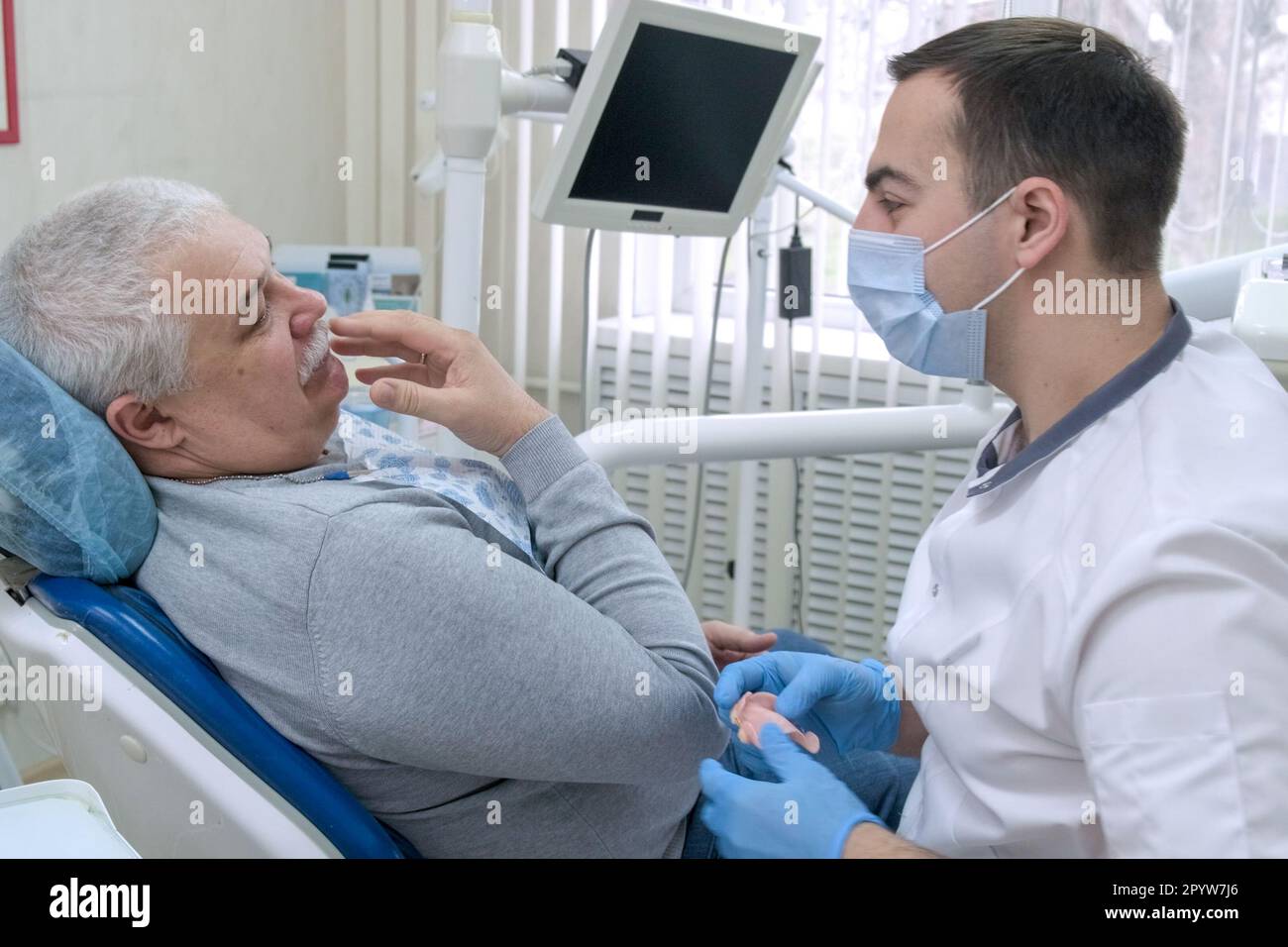 Elderly man sitting in dentist chair talks about his dental problems to ...