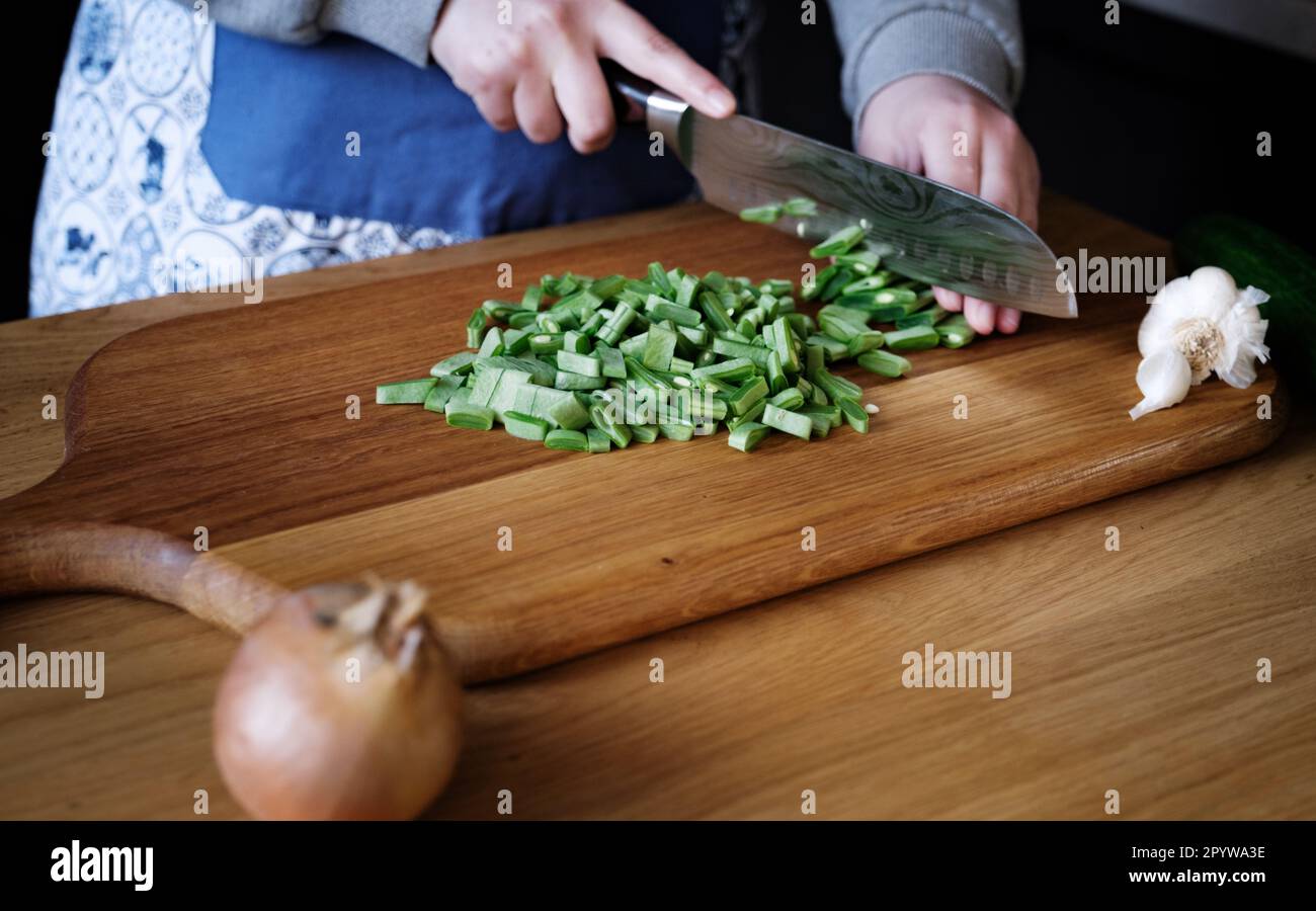 A close-up of a person cutting green beans into thin slices on a ...