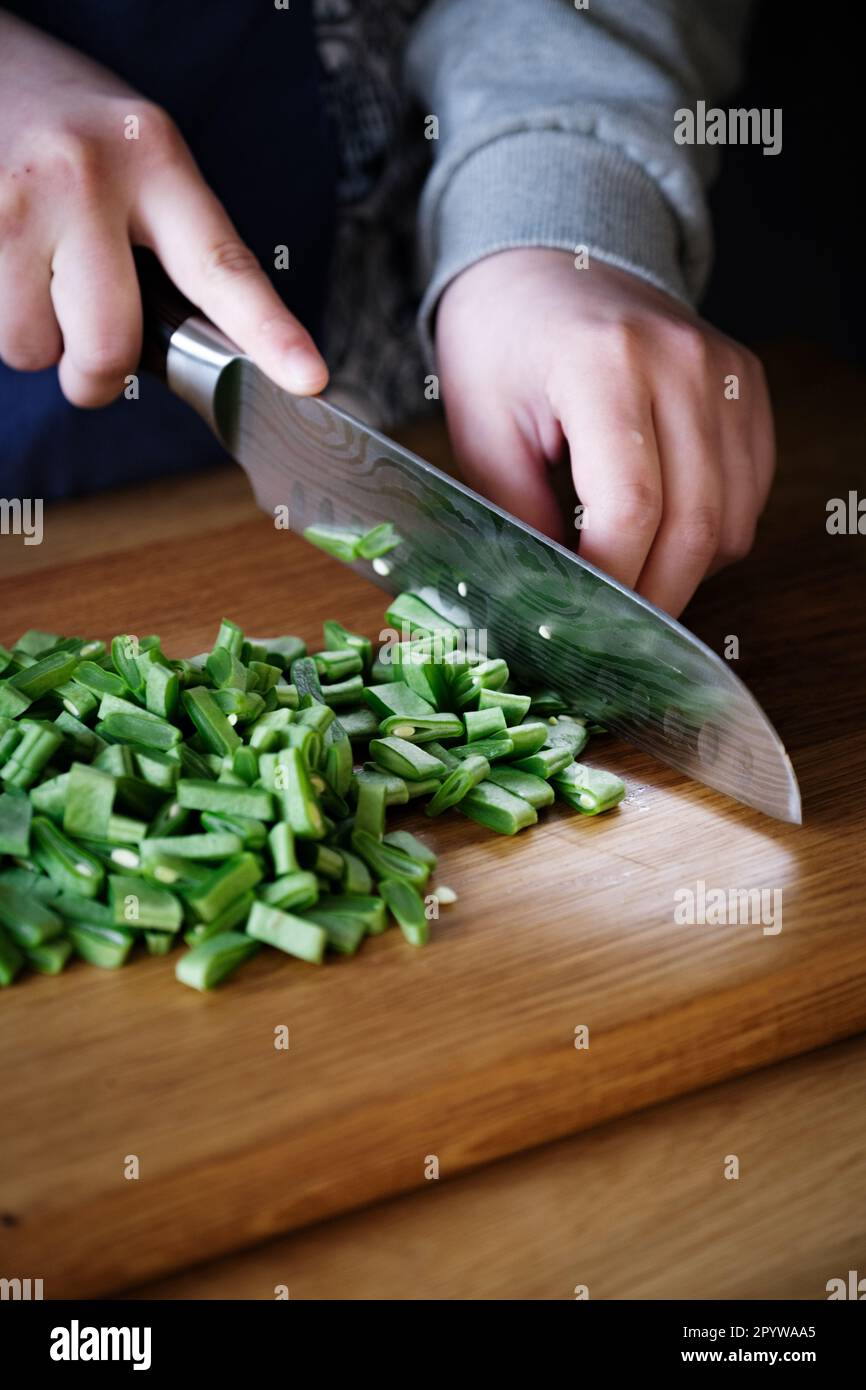 A close-up of a person cutting green beans into thin slices on a ...