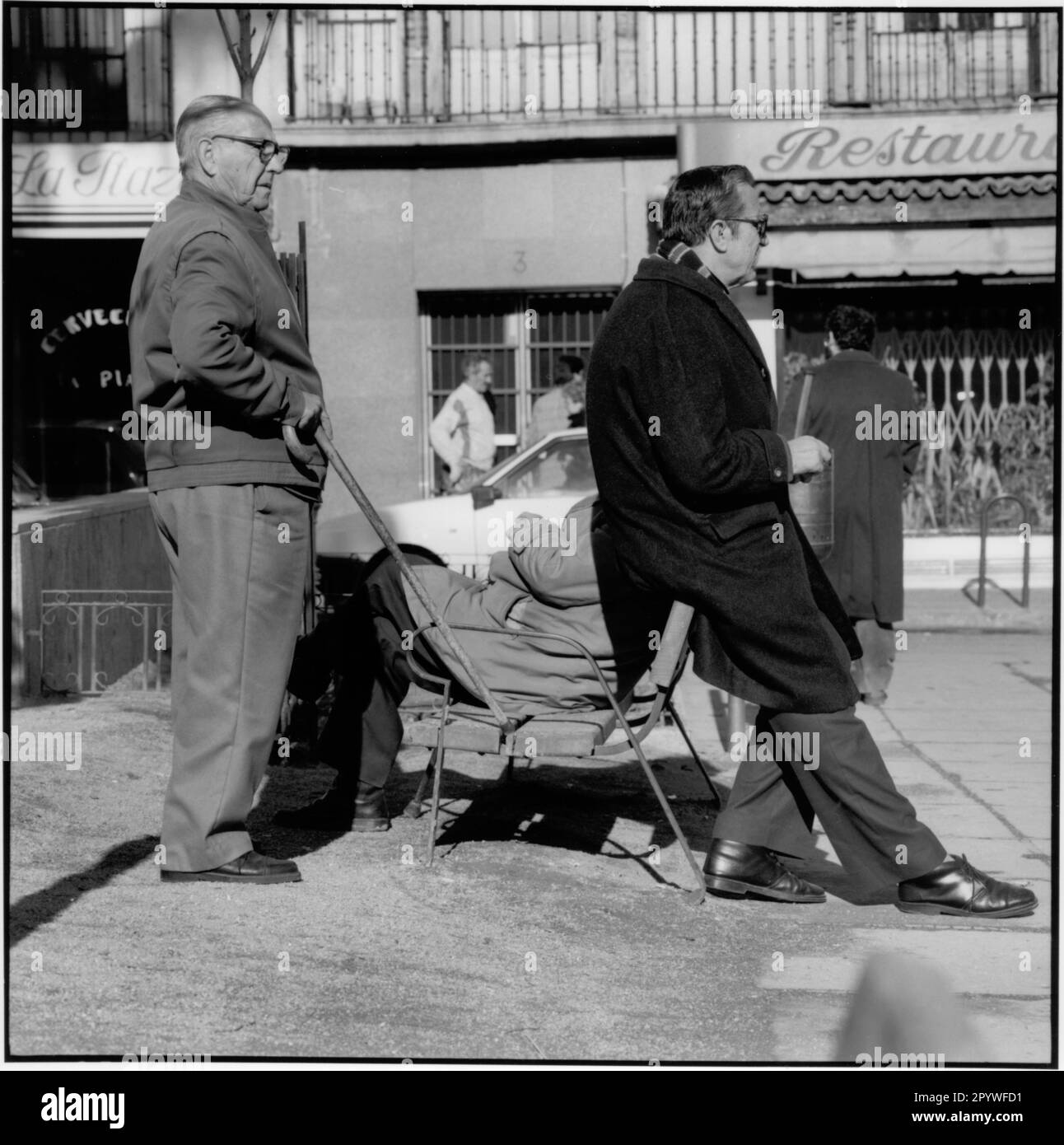 Spain, Madrid. Men wait at a bench in winter. Street scene, black and ...