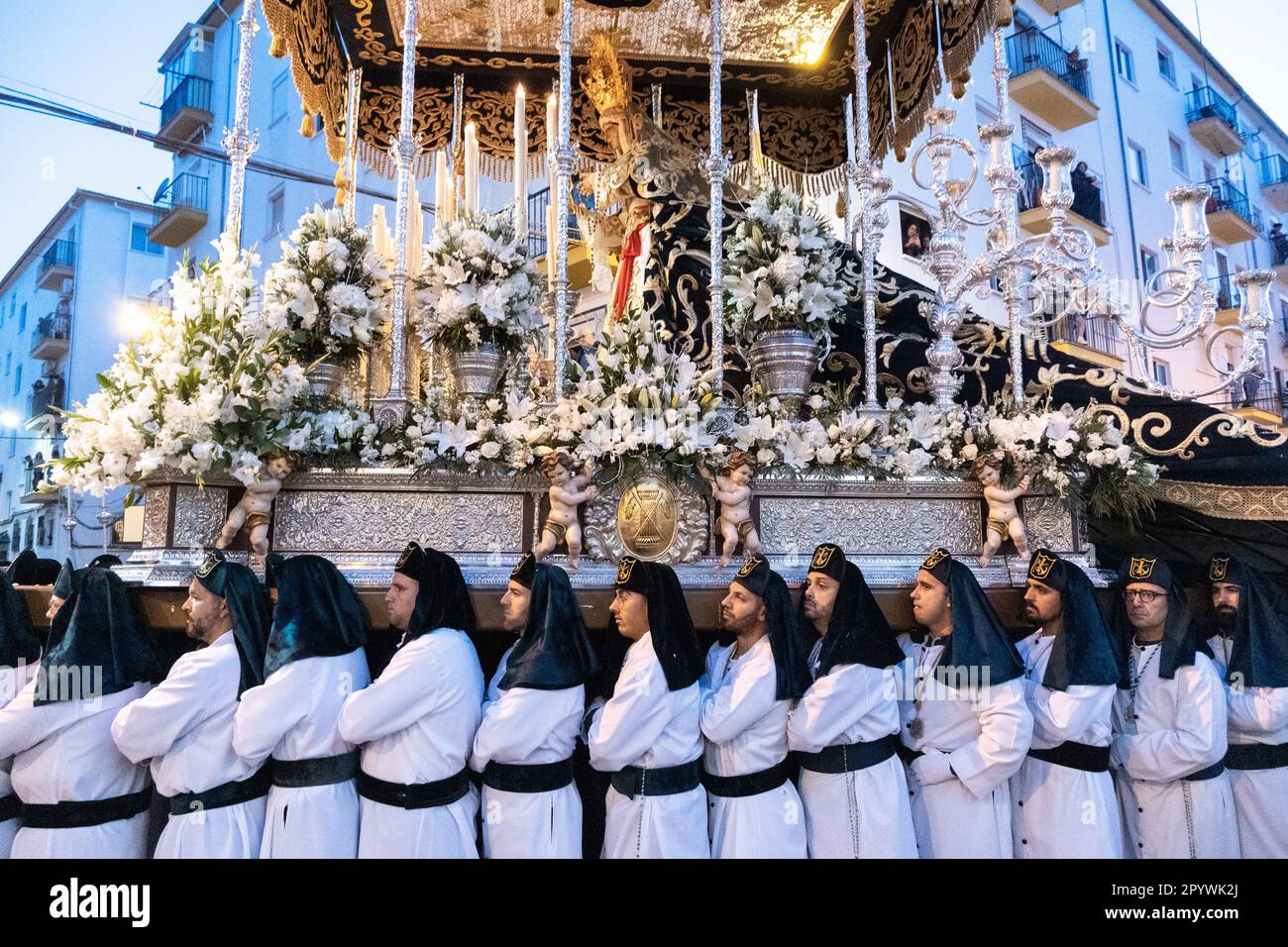 Nazarenos wearing green hats carry a massive platform with a statue of ...