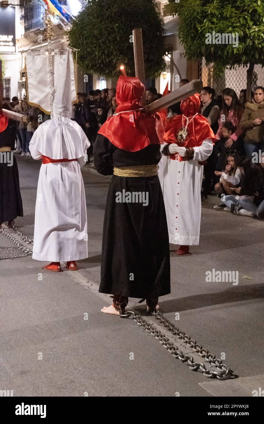 Hooded penitents walk barefoot with chains as they carries wooden ...