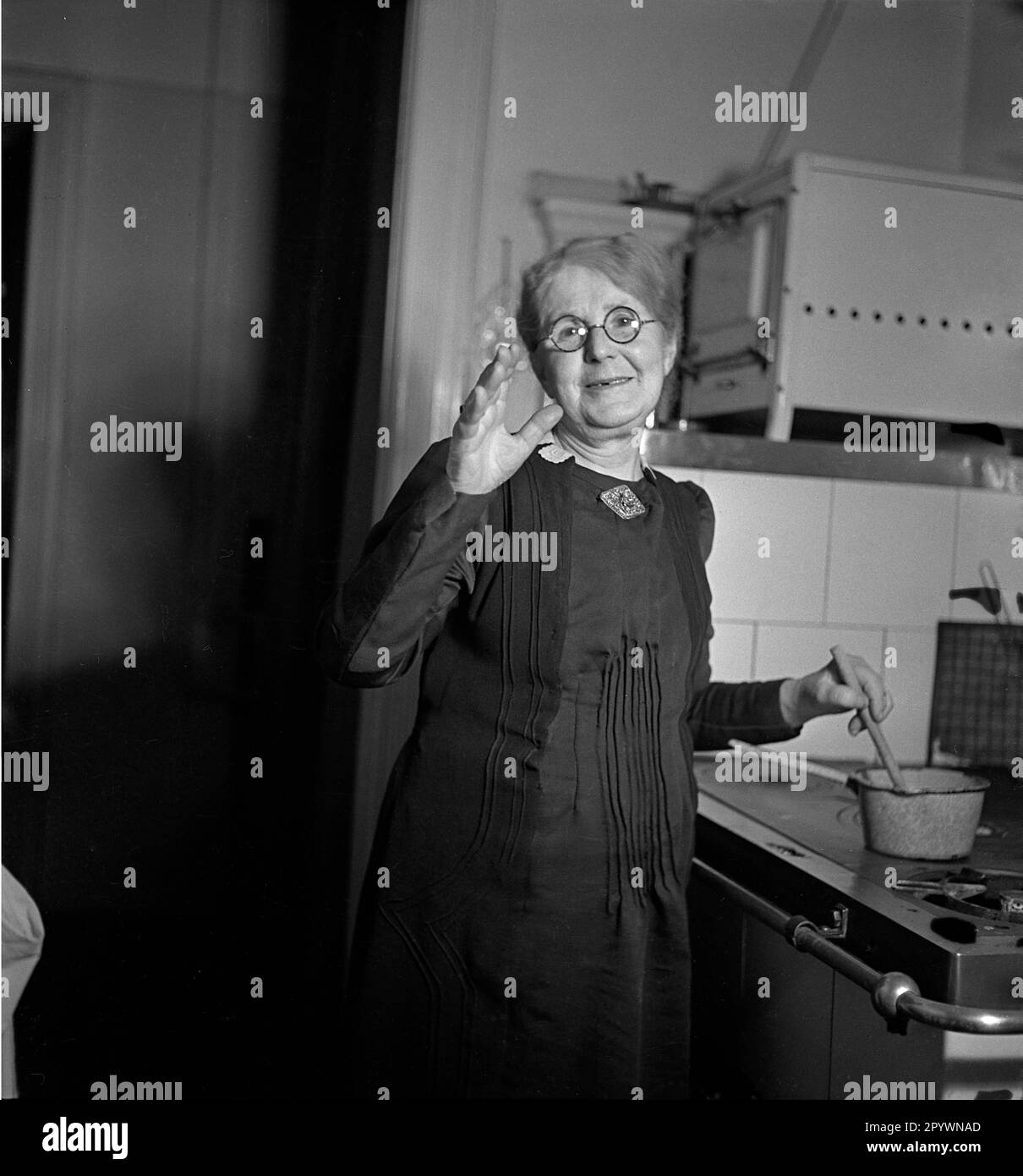An old woman cooks at the stove and waves to the photographer Stock ...