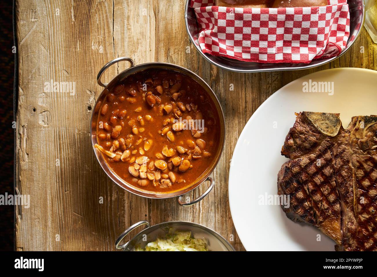 A wooden dining table with delicious steak and baked beans Stock Photo ...
