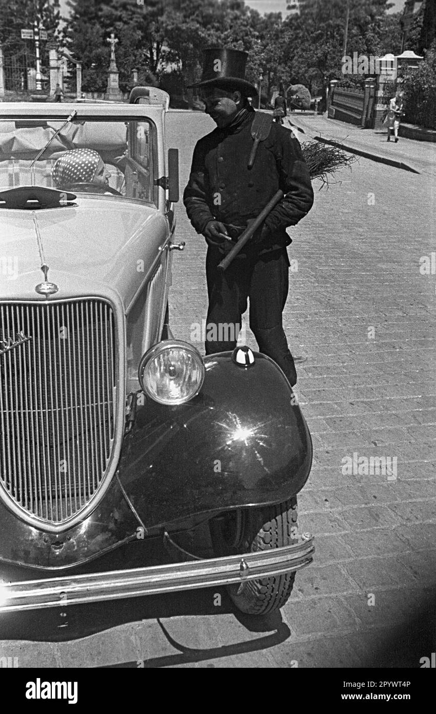 A woman at the wheel of a car talking to a chimney sweep. At ...