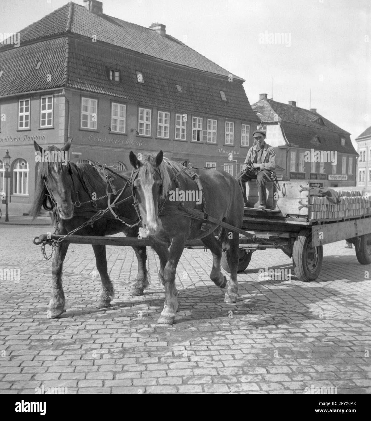 A horse-drawn carriage loaded with bricks crosses a square, presumably ...