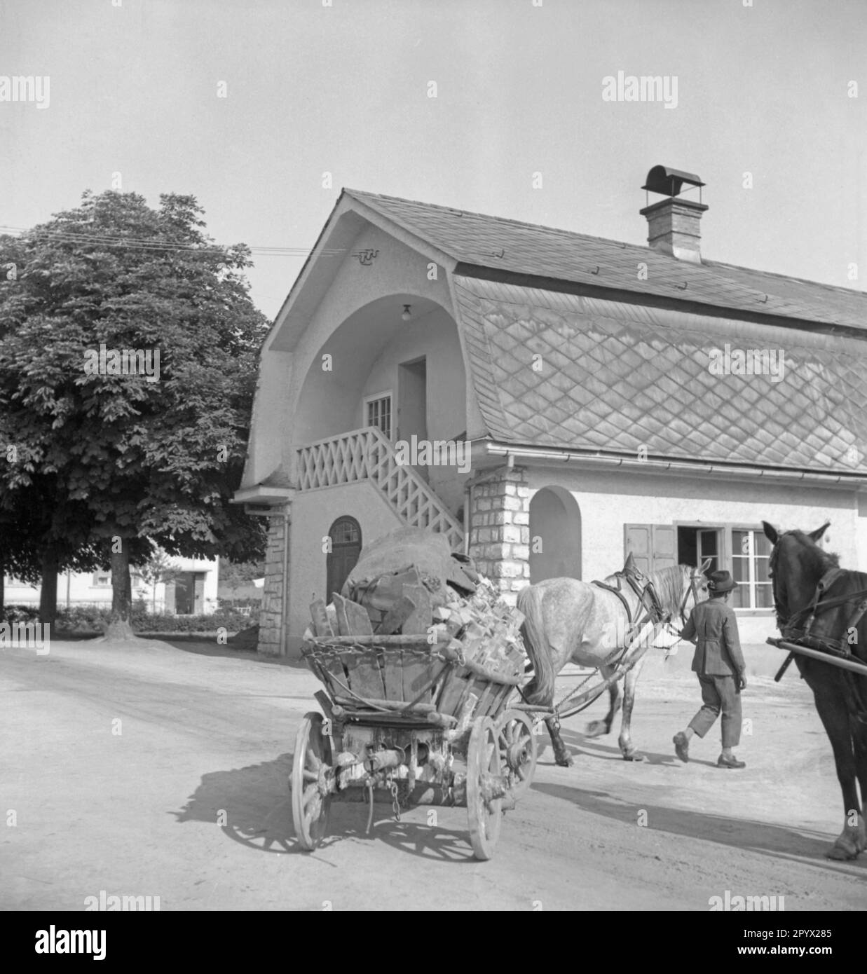 Two horse-drawn carts in front of a house with mansard roof next to ...