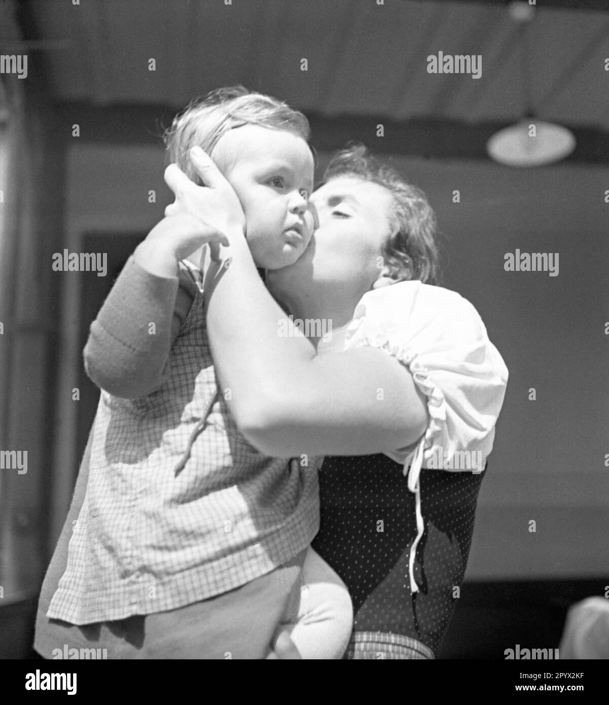 A woman holds a child on her arm and gives him a kiss on the cheek ...