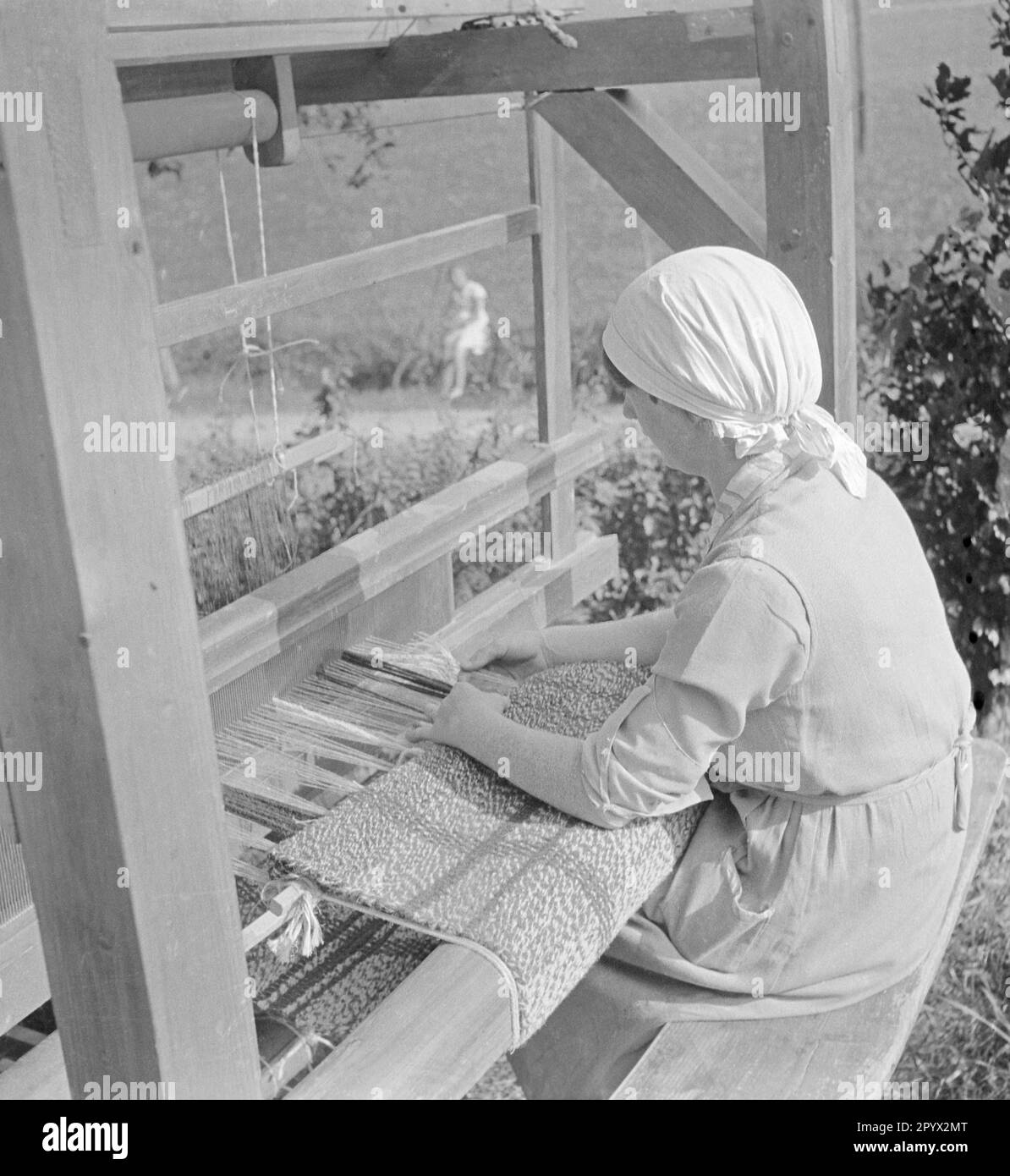 A woman works on a loom in front of the weaving mill Stock Photo - Alamy