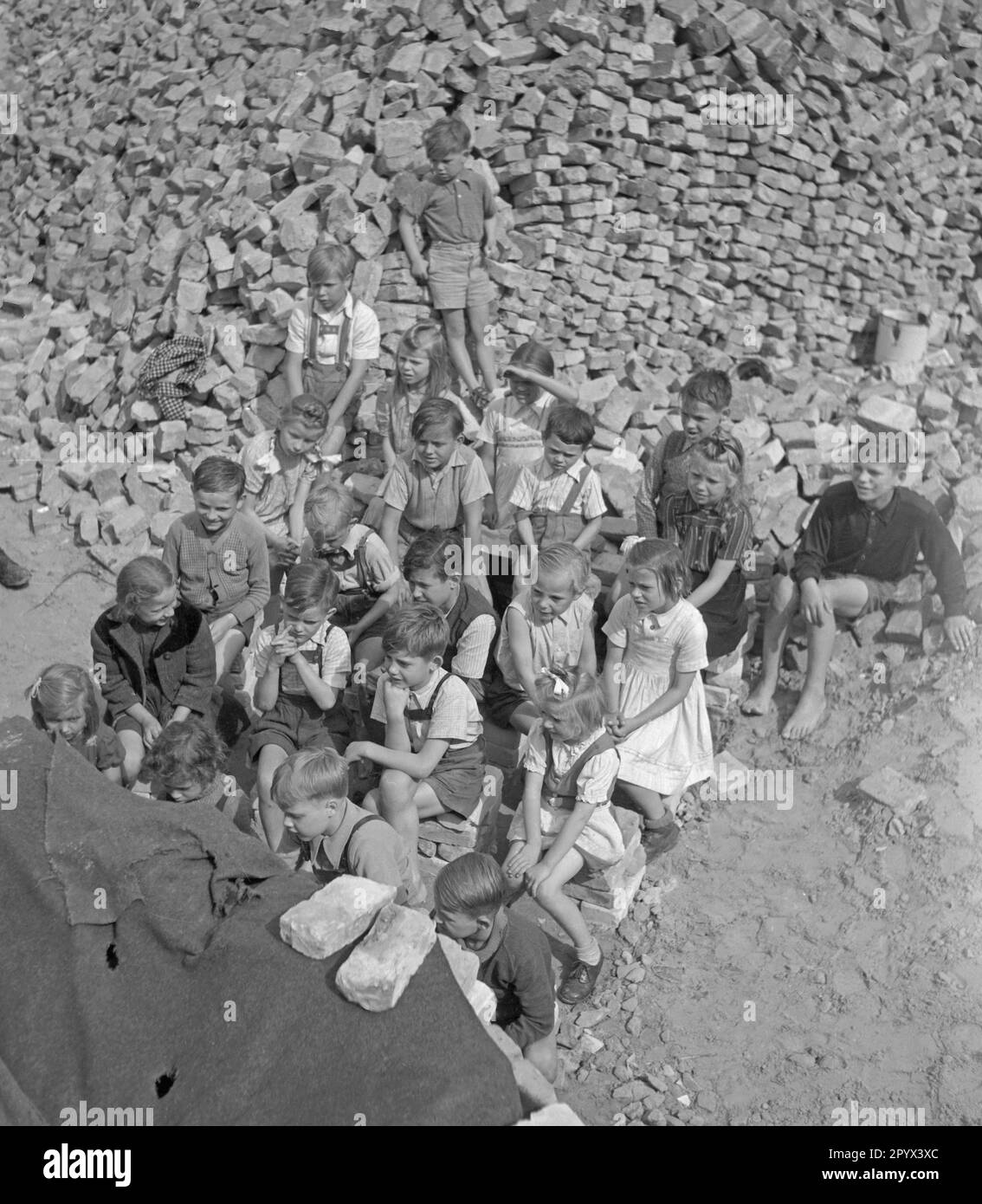Undated photo of a group of children watching a puppet show among piles ...