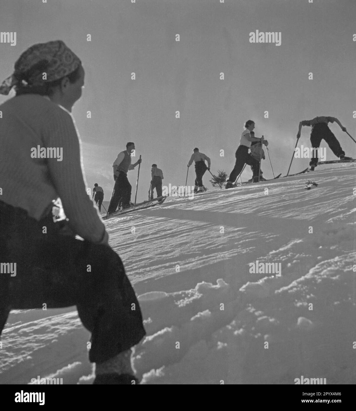 "A woman looks at a group of skiers ascending a high alpine pasture in ...