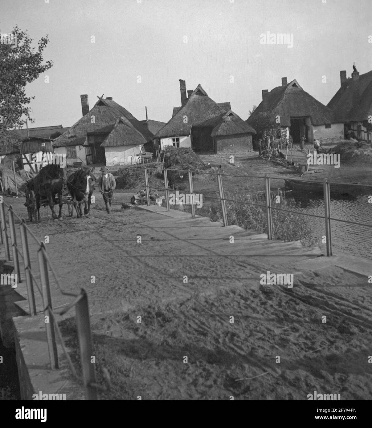 A farmer leads a horse-drawn carriage over a bridge at a village on the ...