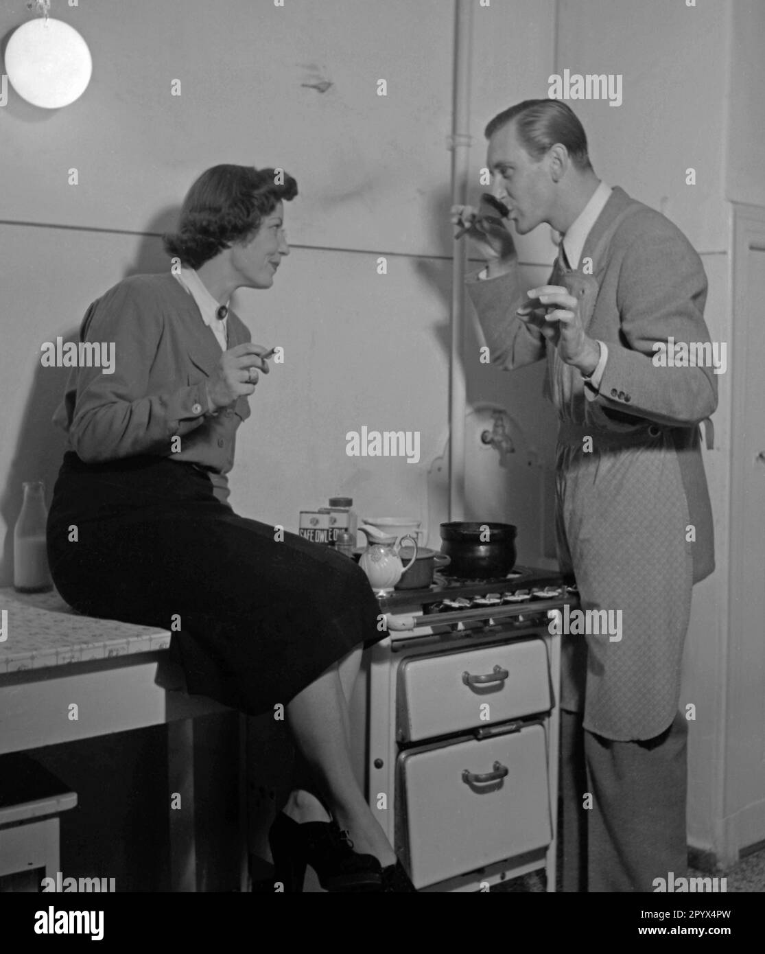 Man and woman in the kitchen at the stove. Undated picture, probably ...