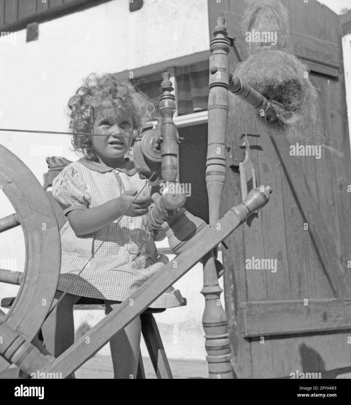 A girl plays with a spinning wheel in a village on the Baltic coast in ...