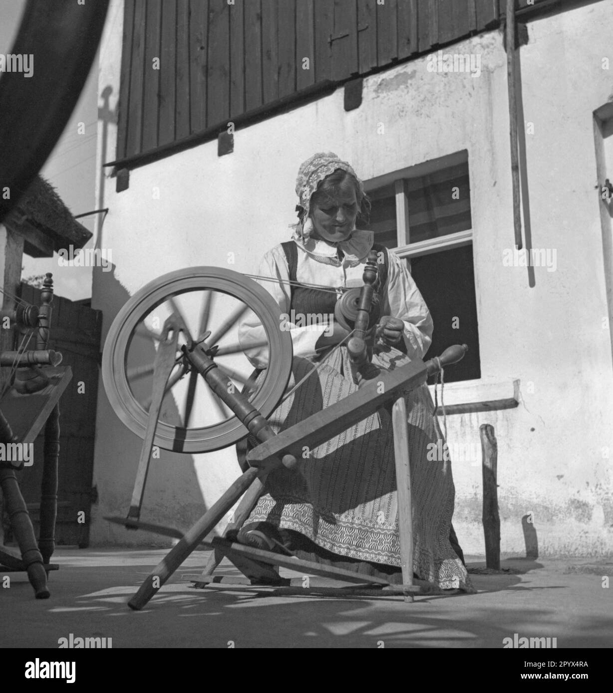 A woman spins on a spinning wheel in a village on the Baltic coast in ...