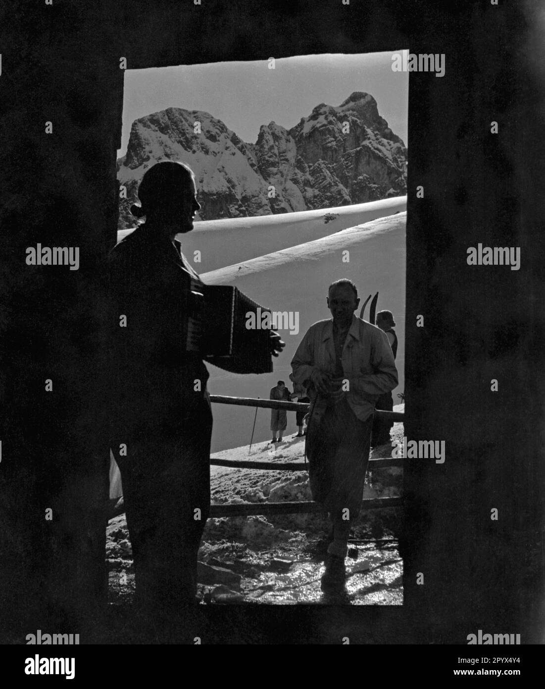 "A man playing on an accordion at the entrance of a hut looking out on ...