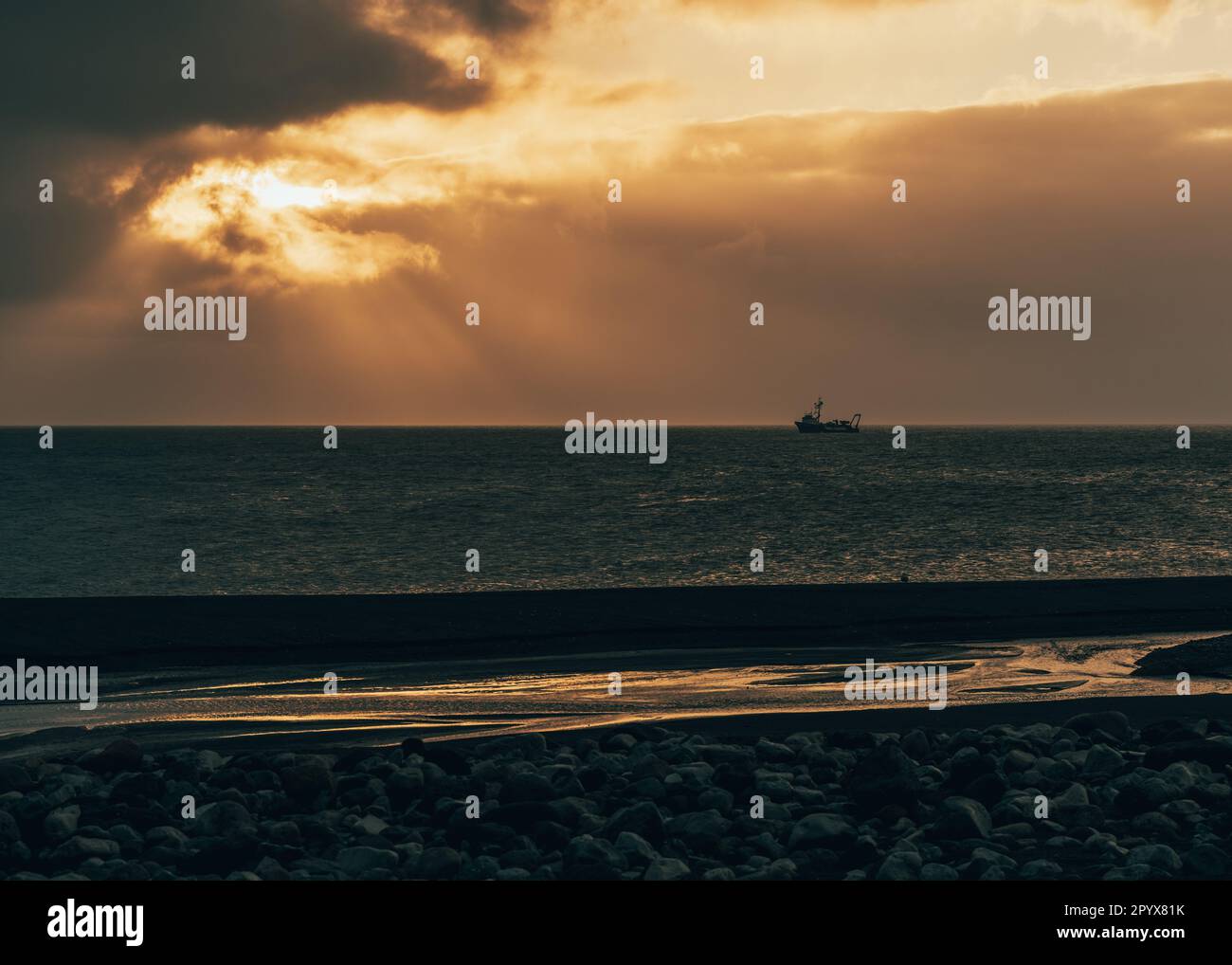 A vibrant sunrise over a fishing boat in Umnak, Alaska, with a beach in ...