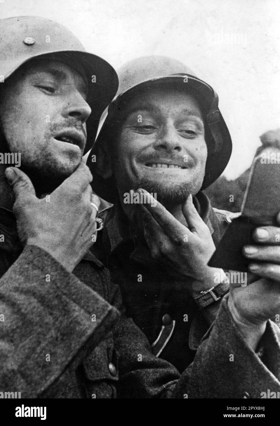 Two infantrymen look at their unshaven faces in a mirror. During the ...