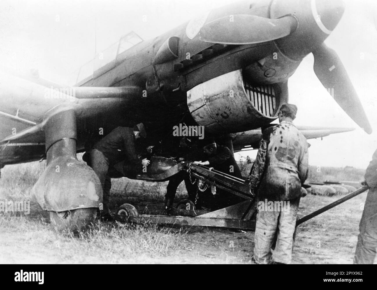 "Ground crew hangs an aerial bomb under the fuselage of a Junkers Ju 87 ...
