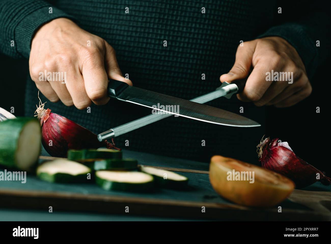a man steels a kitchen knife with a honing steel at a table with some ...
