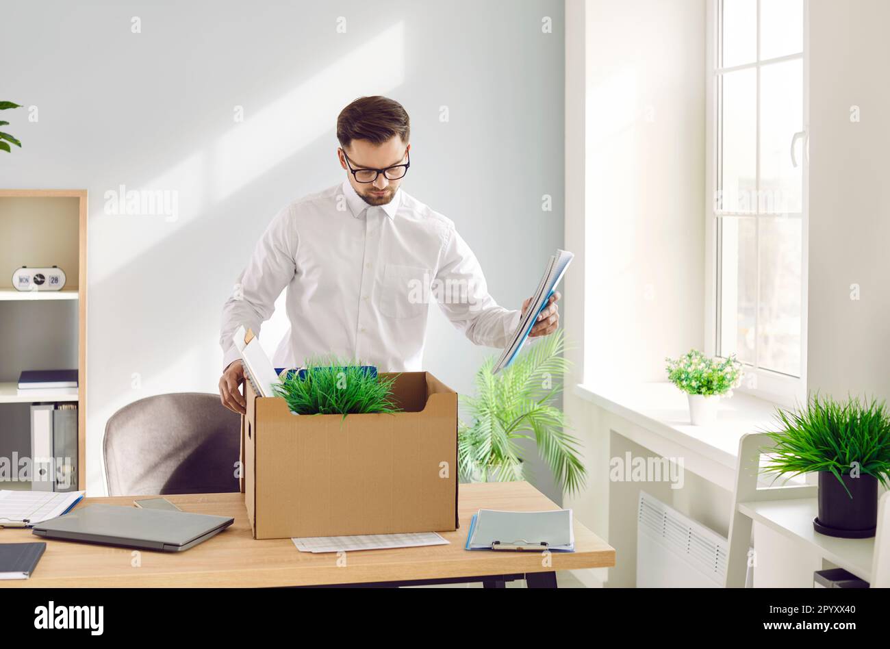 Sad, fired young corporate employee packing stuff off his desk in a ...