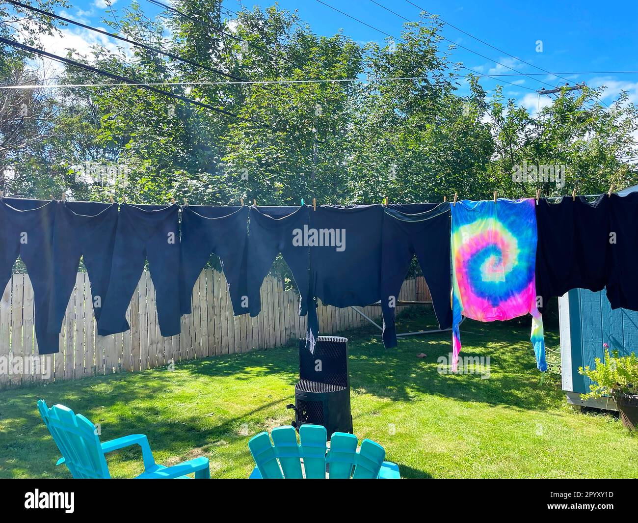 A lone tie dyed shirt on a clothes line hung with black clothes, sunny ...