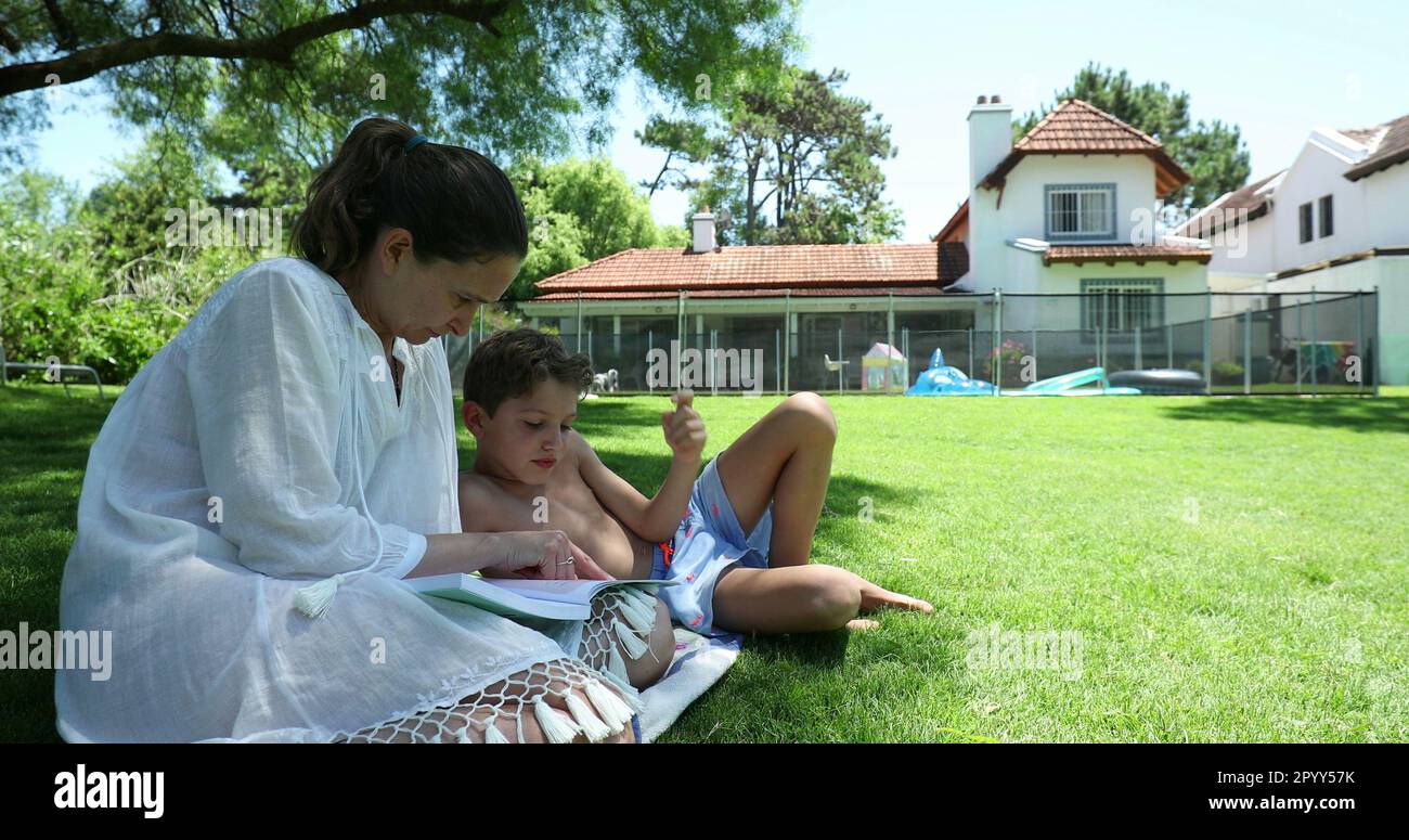 Parent teaching child to read outside. Mother helping kid with homework ...