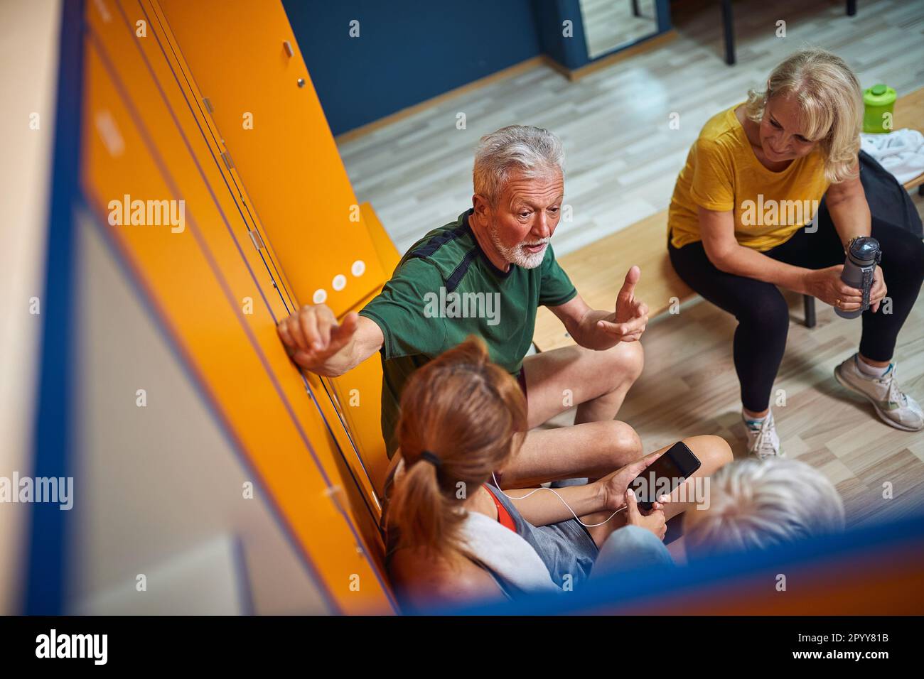 Horizontal top shot of people in gym locker room talking, senior man ...