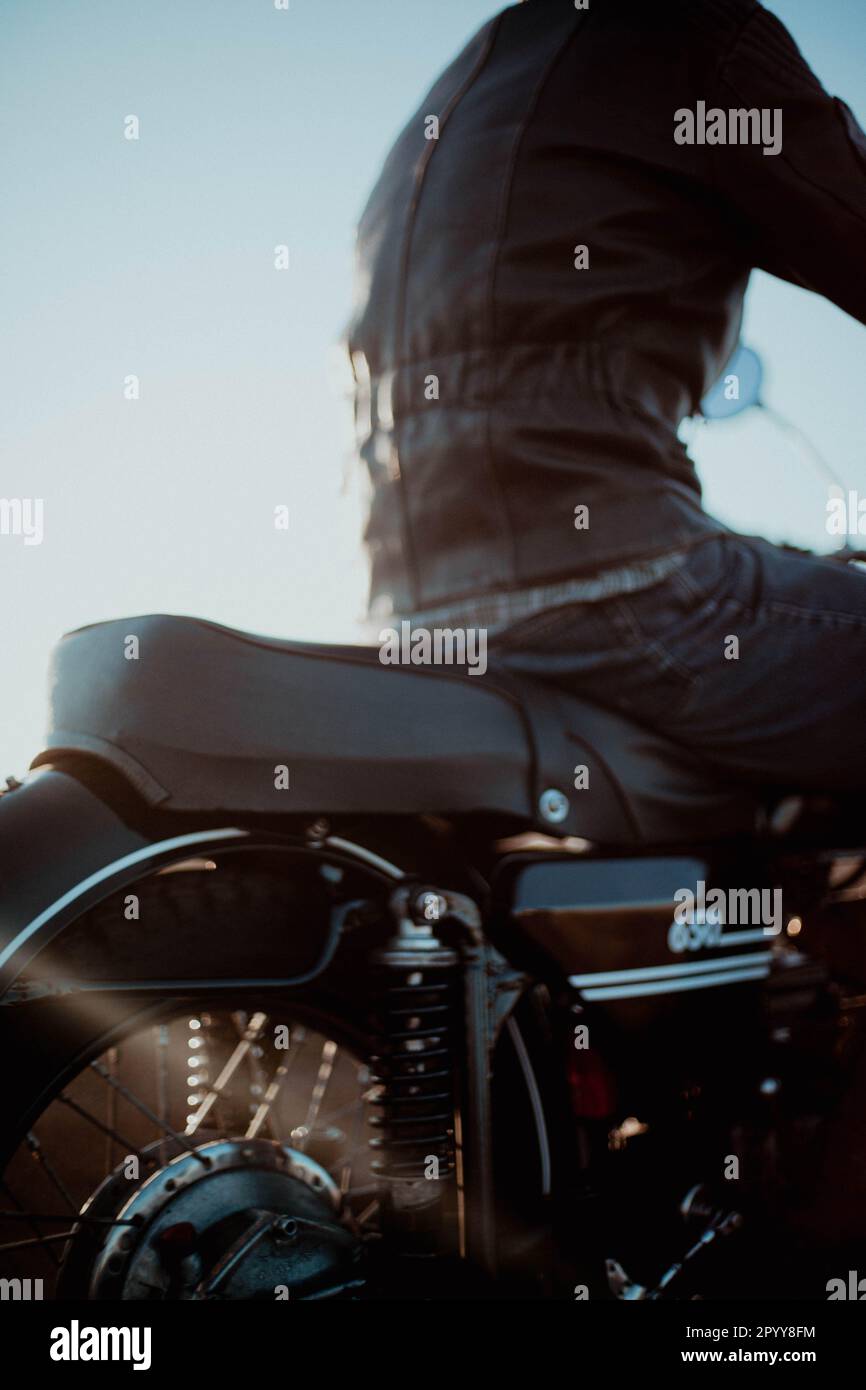 A man wearing a leather jacket and riding a motorcycle on a sunny day ...