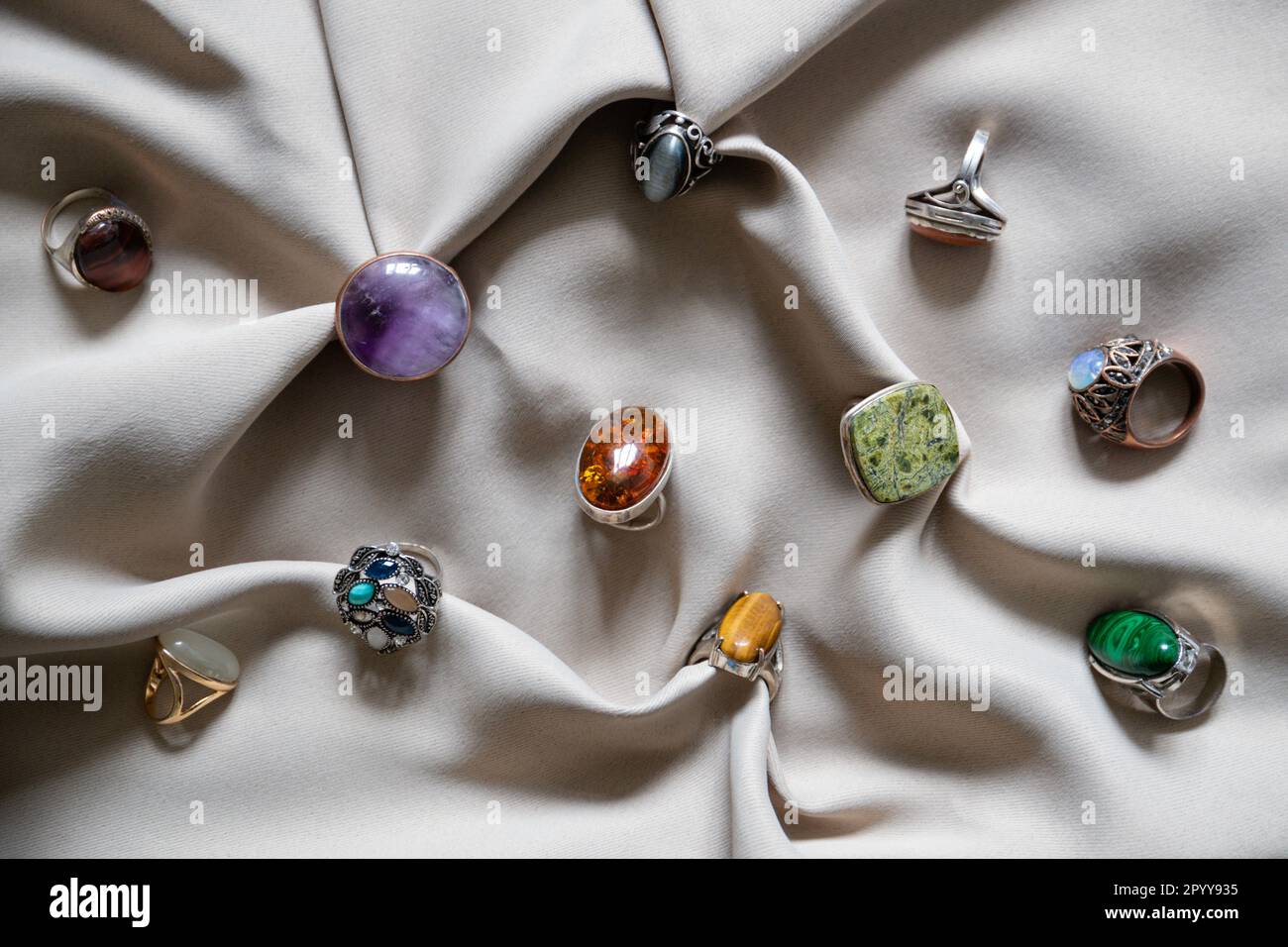 Many different silver rings with various natural gemstones on a beige ...