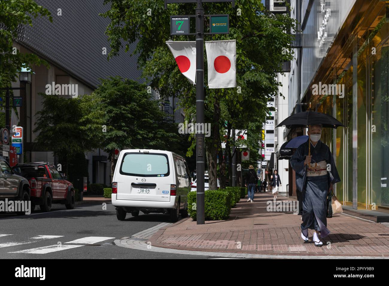 A woman dressed in Kimono with an umbrella walks underneath Japanese flags in Ginza, Tokyo. walk ...