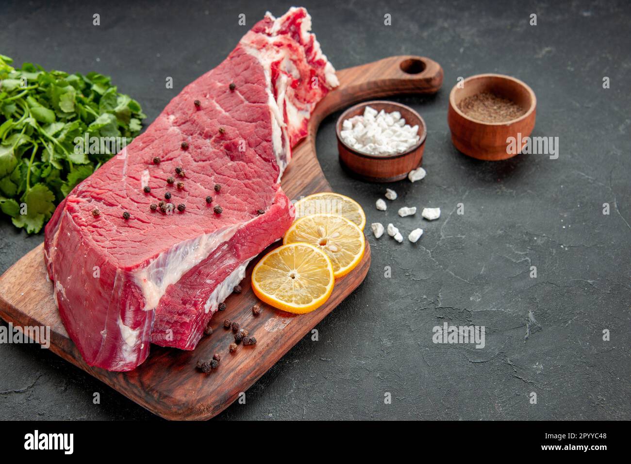front view raw meat slice with lemon slices and seasonings on dark ...