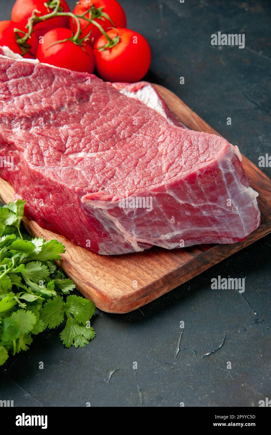 front view raw meat slice with red tomatoes and greens on dark gray ...