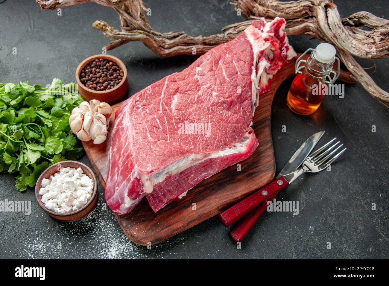 front view raw meat slice with seasonings and greens on dark background ...