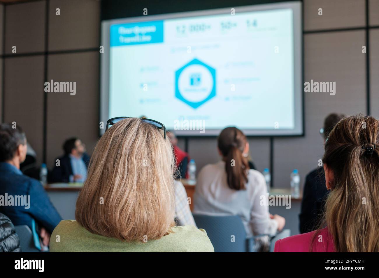 Back view of group of anonymous colleagues sitting near big monitor and ...