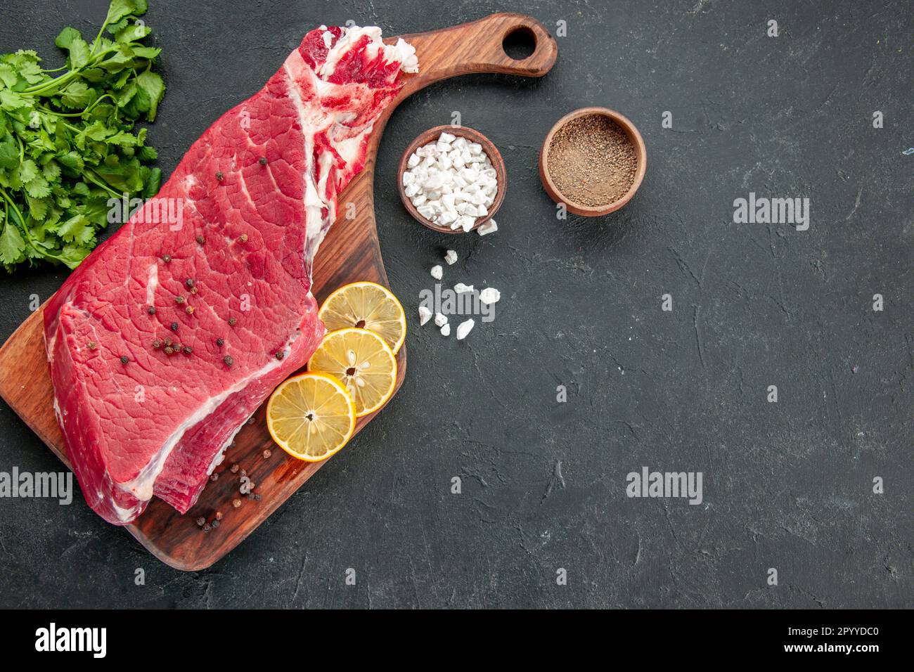 top view raw meat slice with lemon slices and seasonings on dark ...