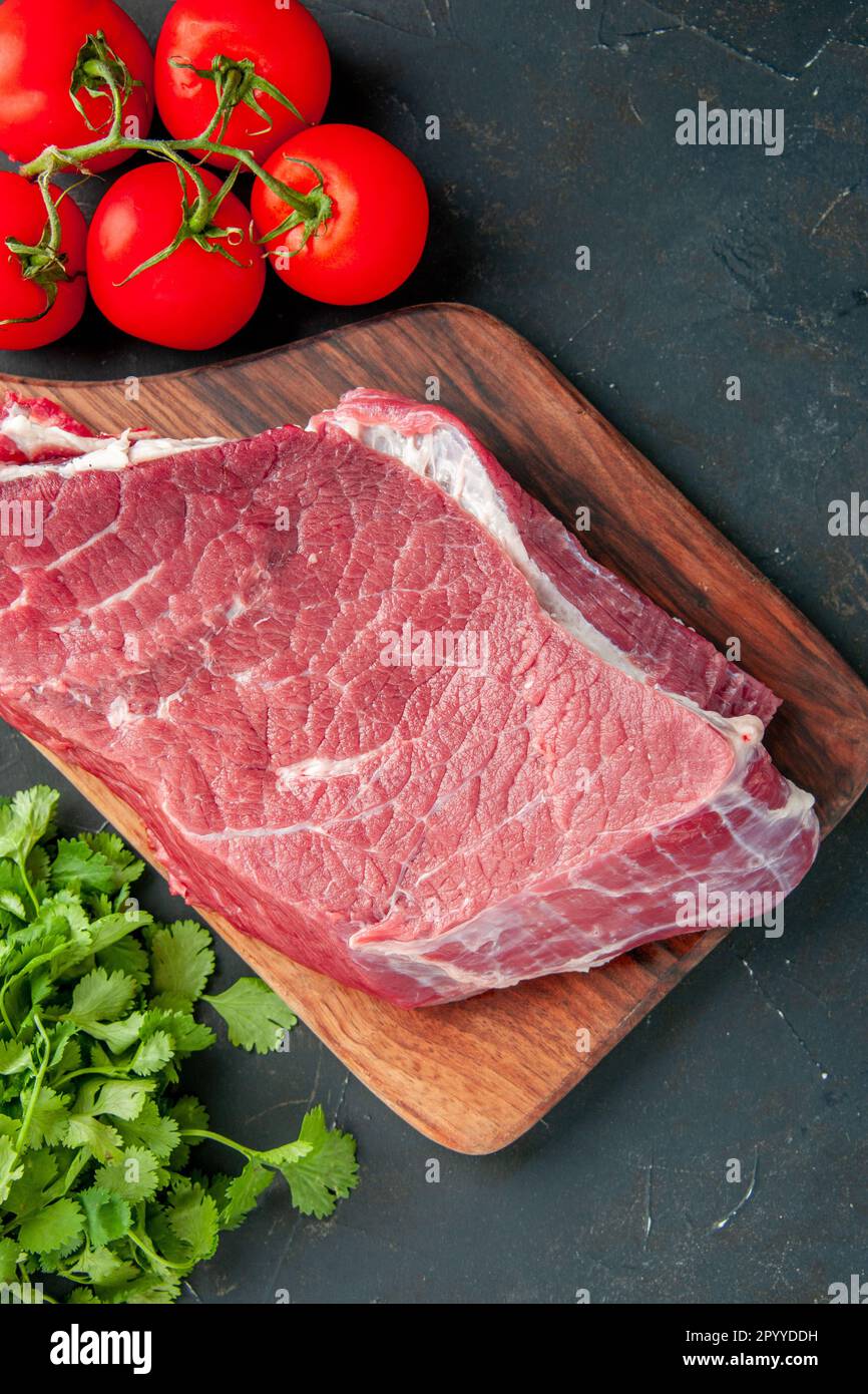 top view raw meat slice with red tomatoes and greens on dark background ...