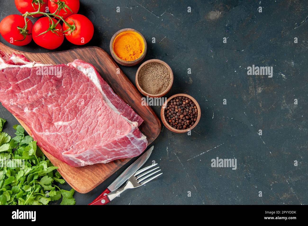 top view raw meat slice with red tomatoes and greens on dark background ...
