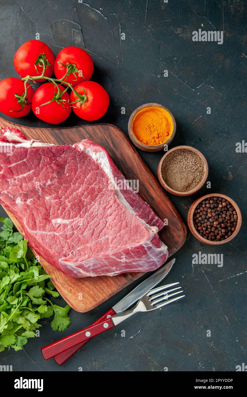 top view raw meat slice with red tomatoes and greens on a dark ...