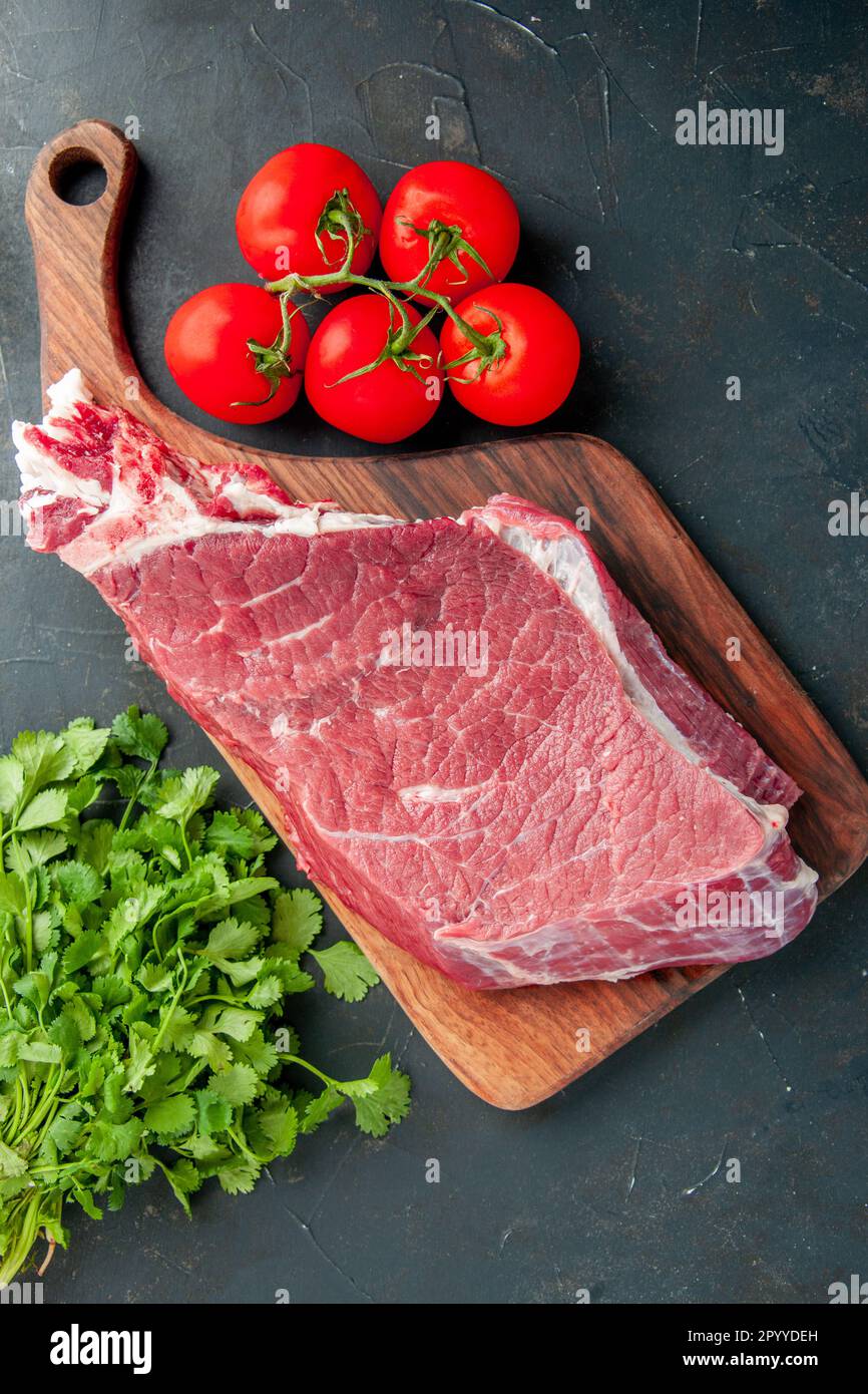 top view raw meat slice with red tomatoes and greens on dark background ...