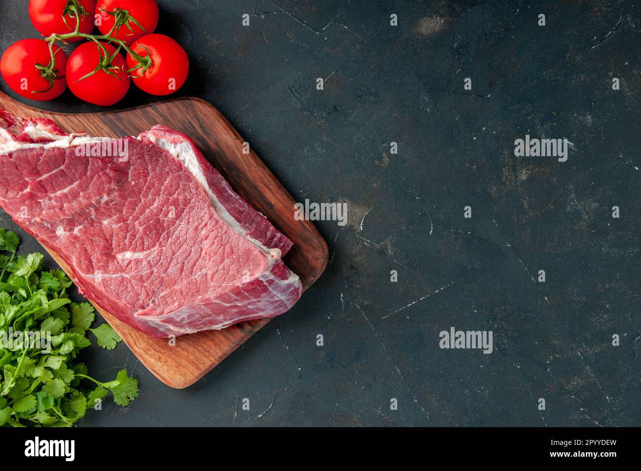 top view raw meat slice with red tomatoes and greens on dark background ...