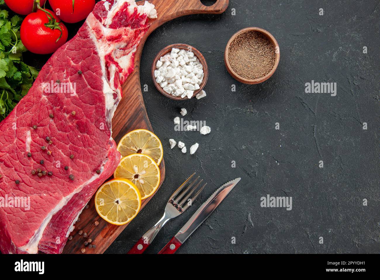 top view raw meat slice with red tomatoes and greens on dark background ...