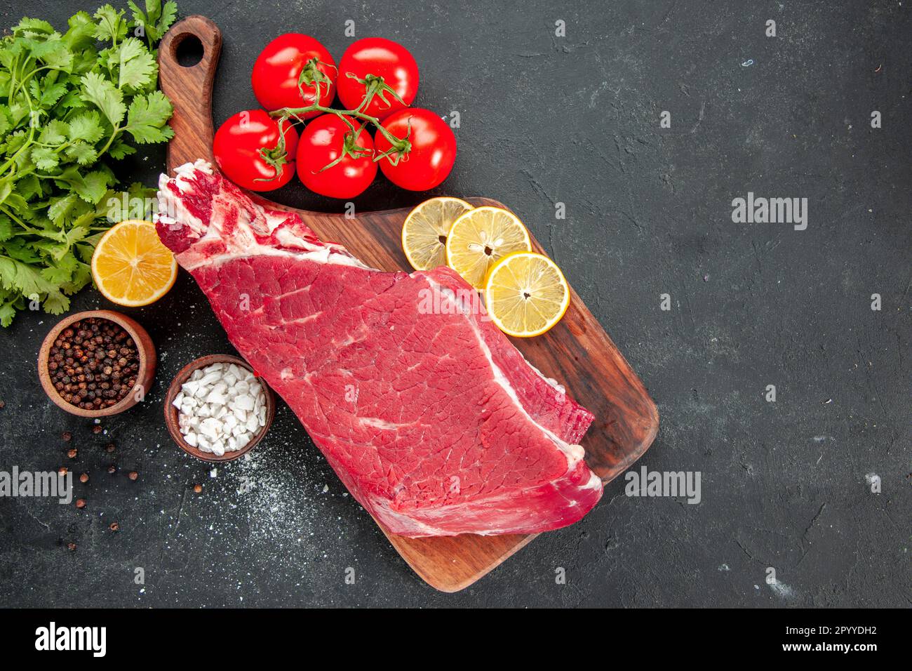 top view raw meat slice with red tomatoes and greens on dark background ...